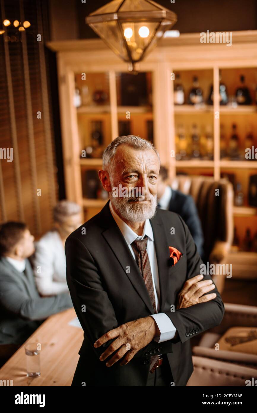 Portrait of handsome smiling old man in black formal suit keeps hands ...