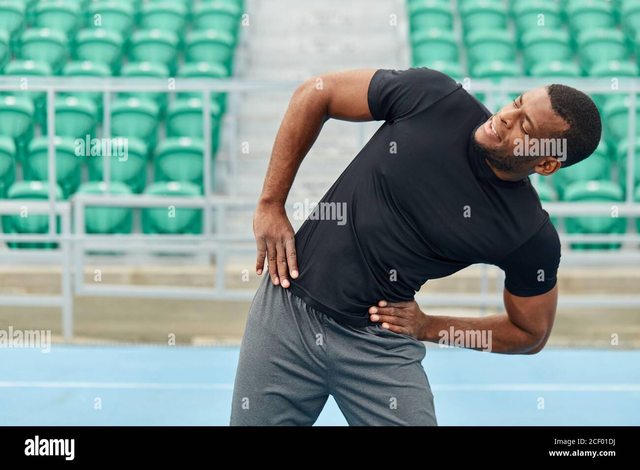 african cheerful sportsman holding arms on the hips doing side bends ...