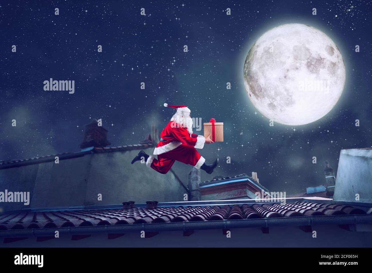 Santa Claus runs fast on a roof with a present Stock Photo - Alamy