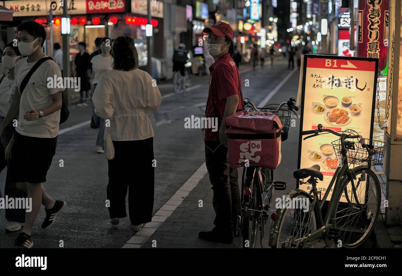 A food delivery person stands on the side of a busy street near ...