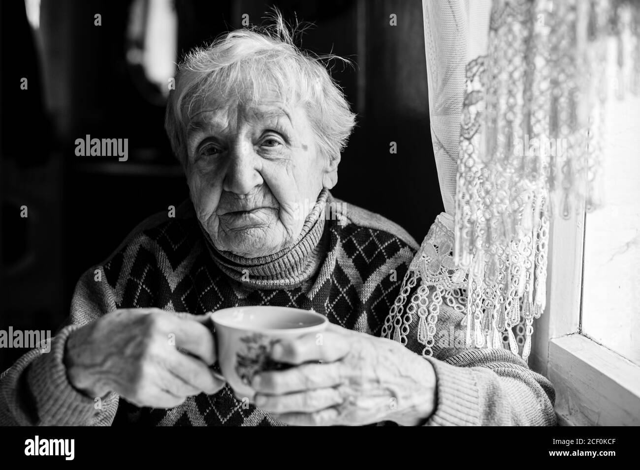 An old woman drinking tea looking out the window. Black and white ...