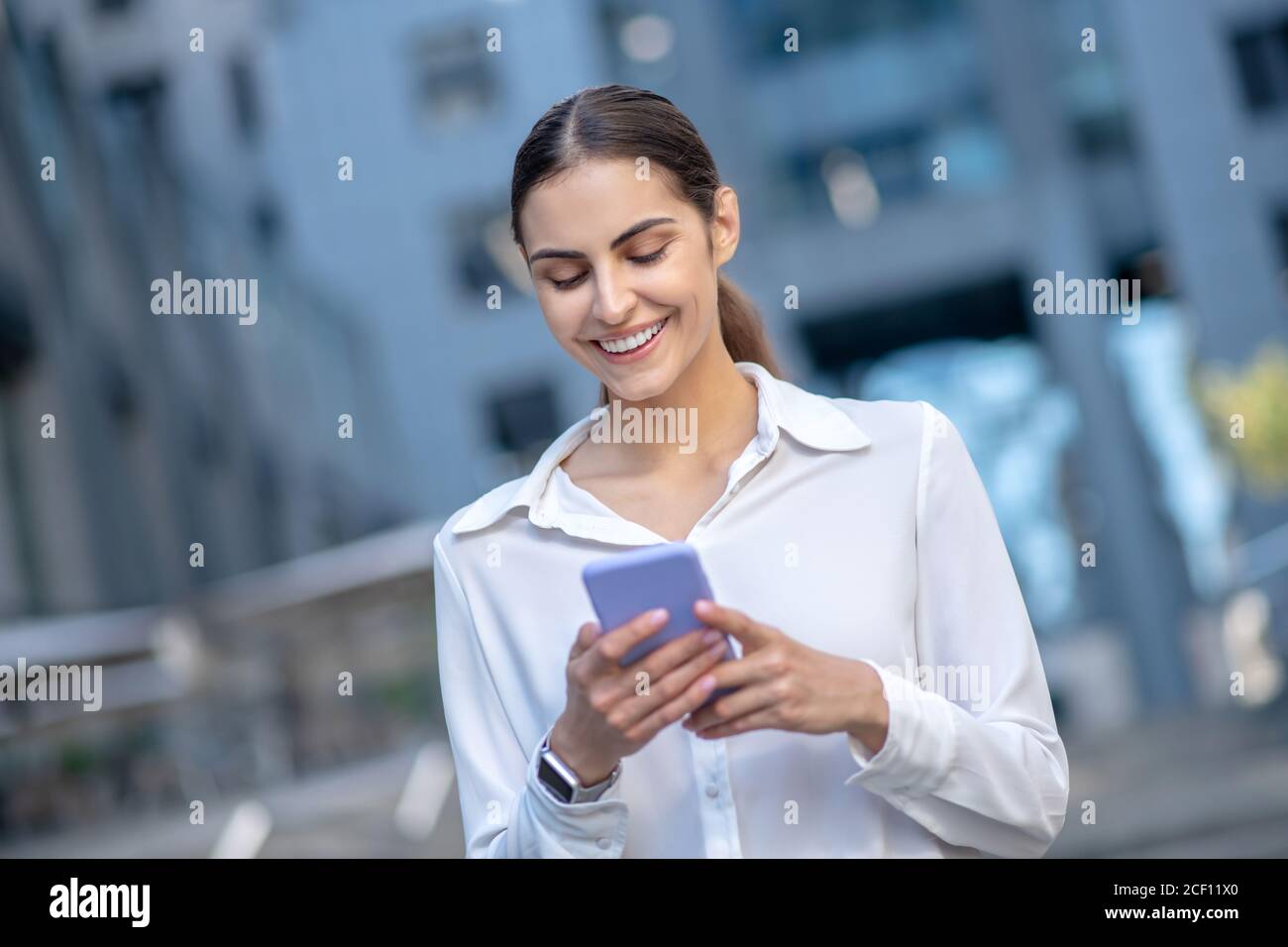 Elegant woman in a white shirt smiling and typing a message Stock Photo ...