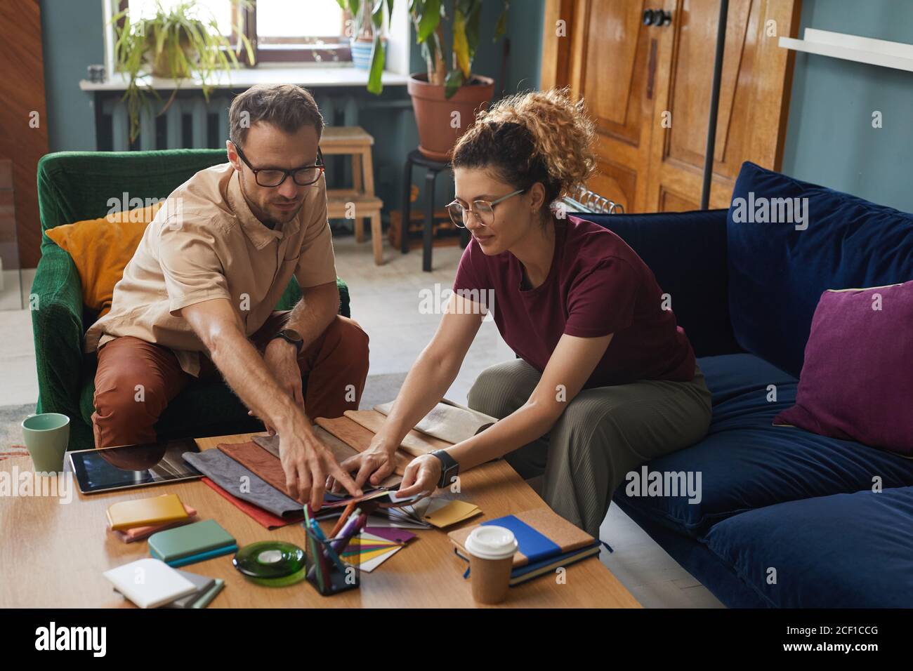 Two designers sitting on sofa and working with samles and patterns in ...