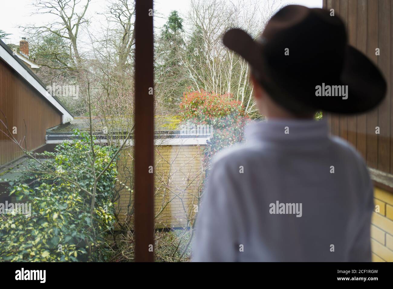 Thoughtful boy in cowboy hat looking out home window Stock Photo - Alamy