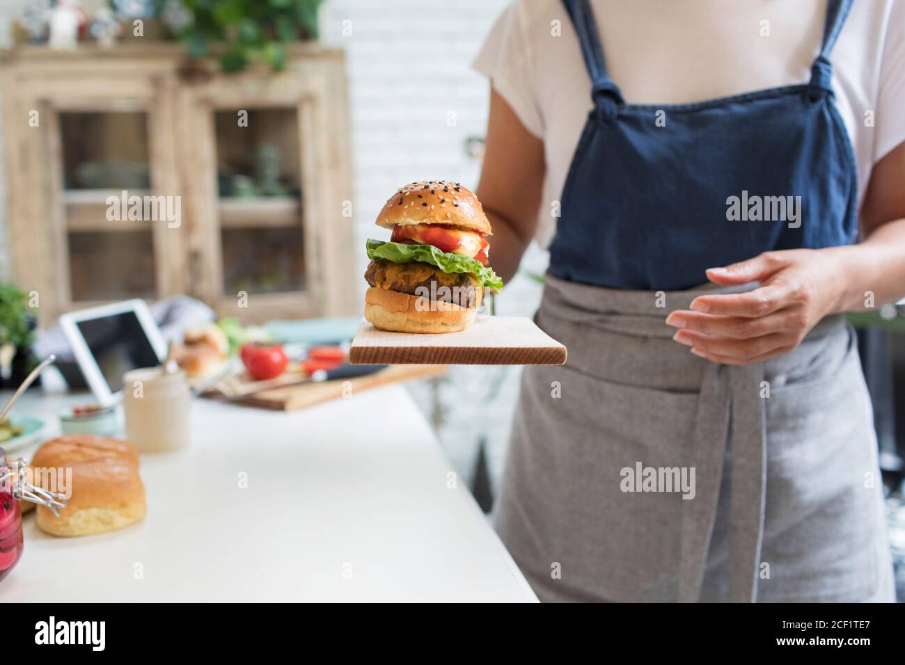 Woman serving hamburger on cutting board in kitchen Stock Photo - Alamy