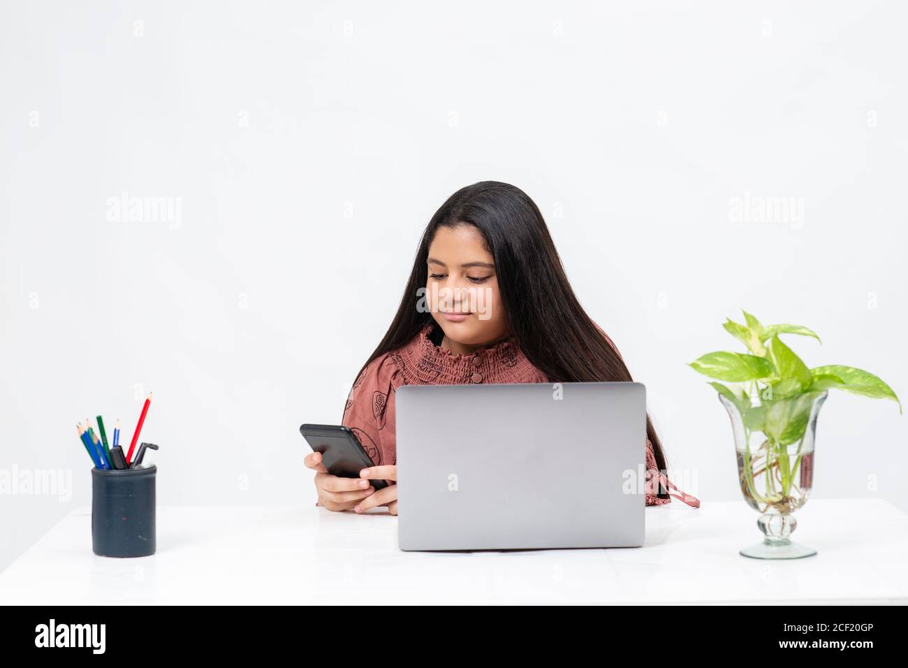 Portrait of a smiling young Indian girl using her phone as she sits ...