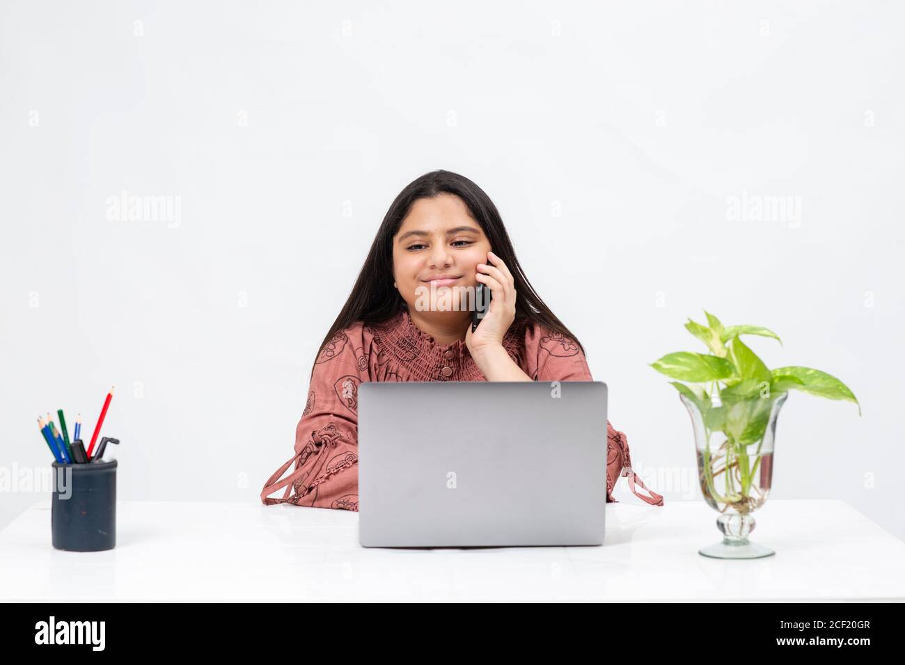 Portrait of a smiling young Indian girl using her phone as she sits ...