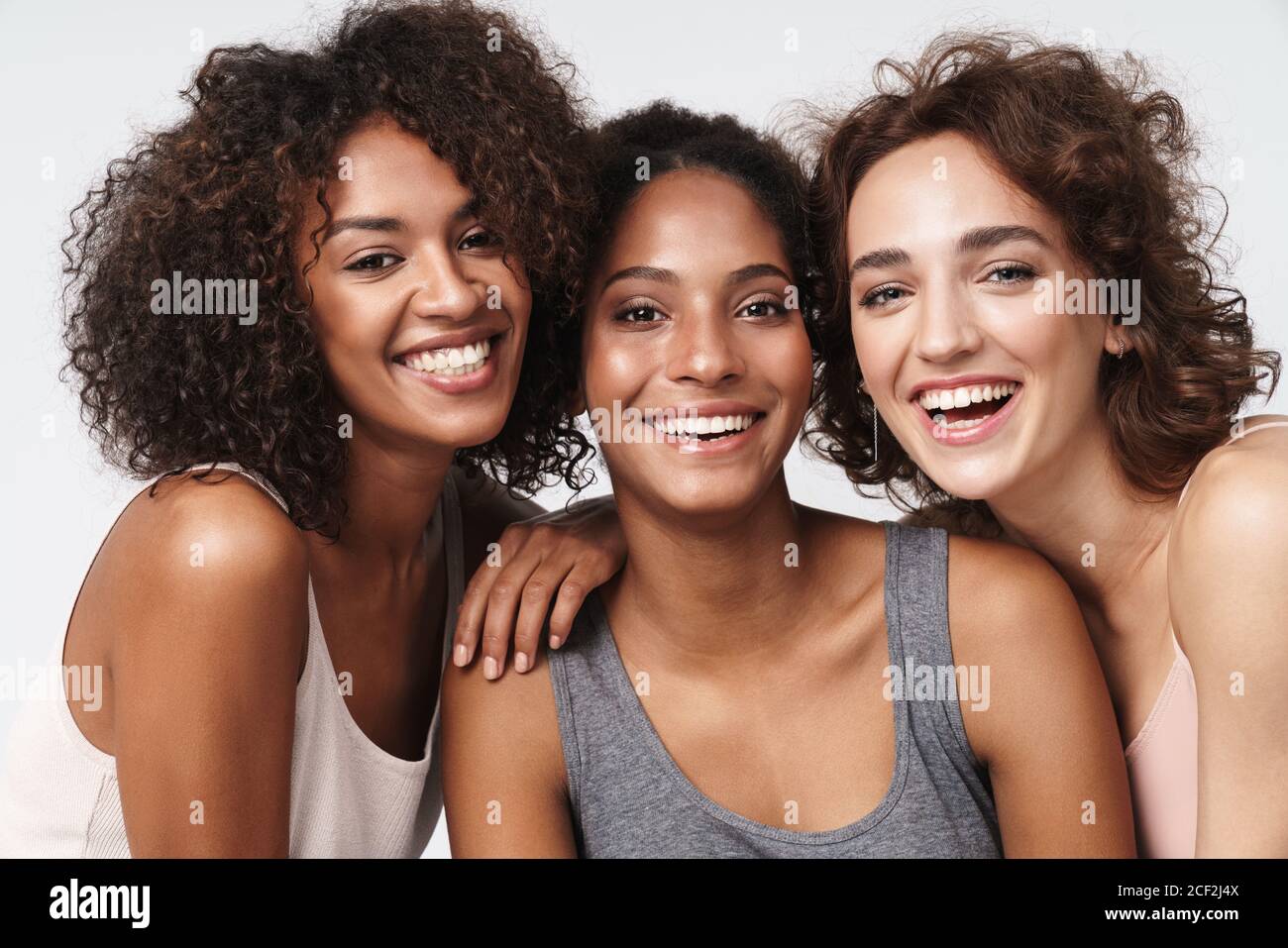 Portrait of three young multiracial women standing together and smiling ...
