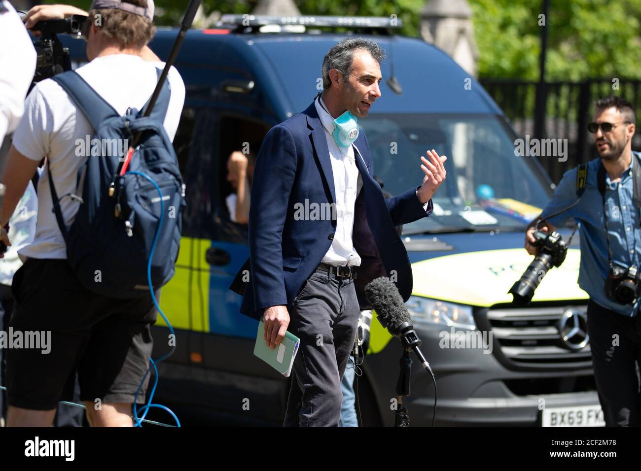 A journalist gives a report to camera next to a police van at an ...