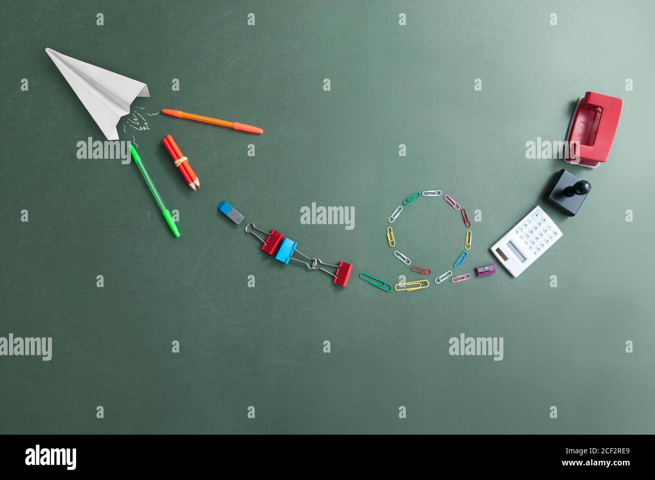 Trail of stationery with a loop behind a paper airplane on a green ...