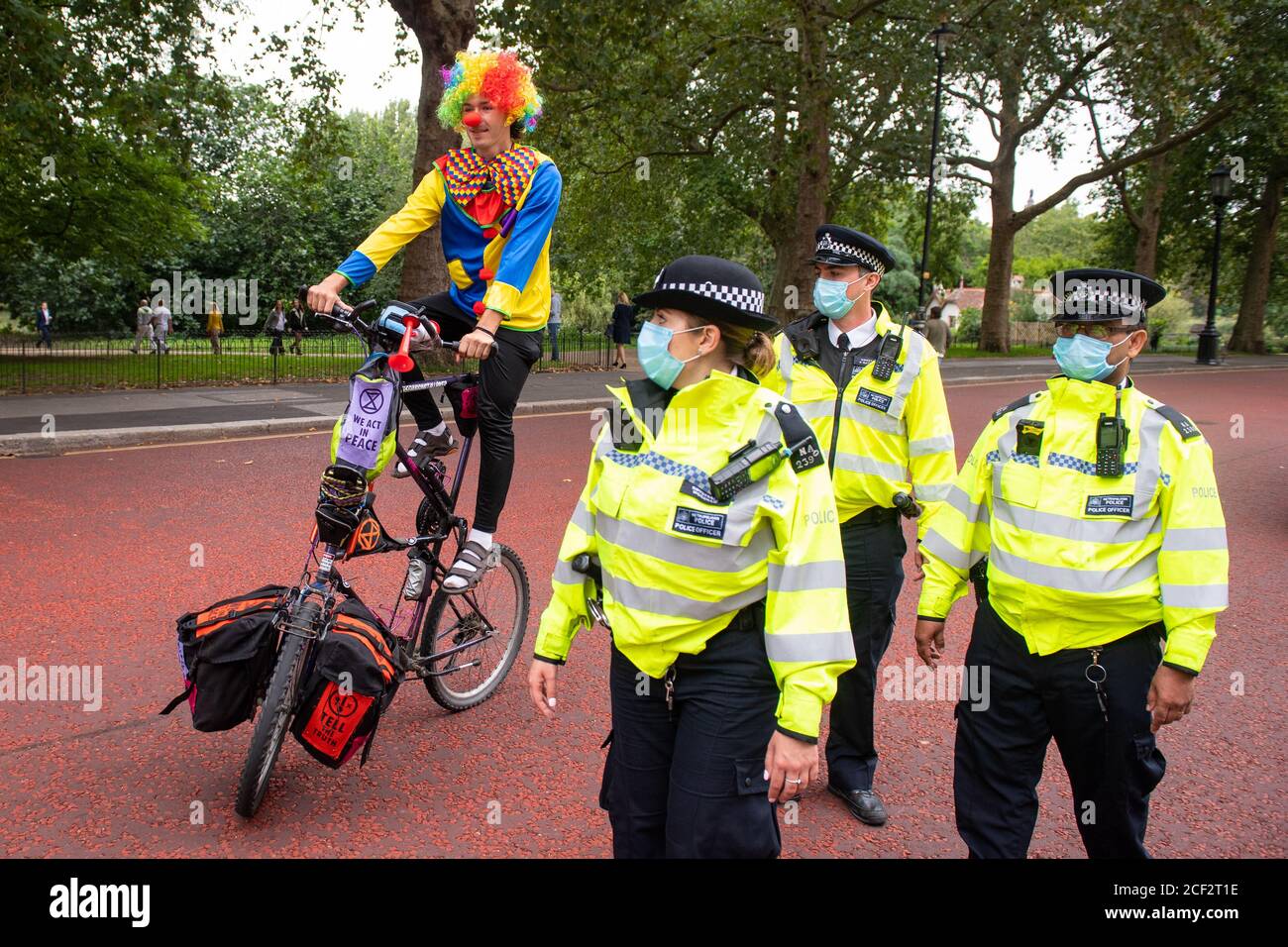 A protestor dressed as a clown rides an oversized bike past police ...