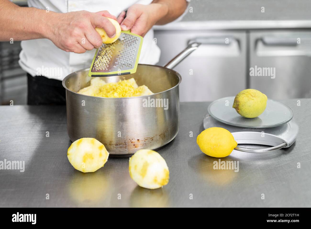 A Pastry chef's hand grates lemon in commercial kitchen. Chef grates ...