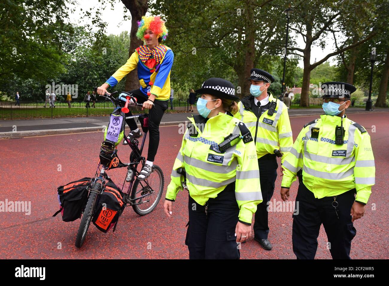 A demonstrator dressed as a clown rides a bike past police officers ...