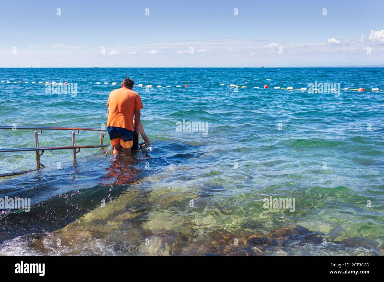 Man on wheelchair on accessible beach with ramp. Disabled person going ...