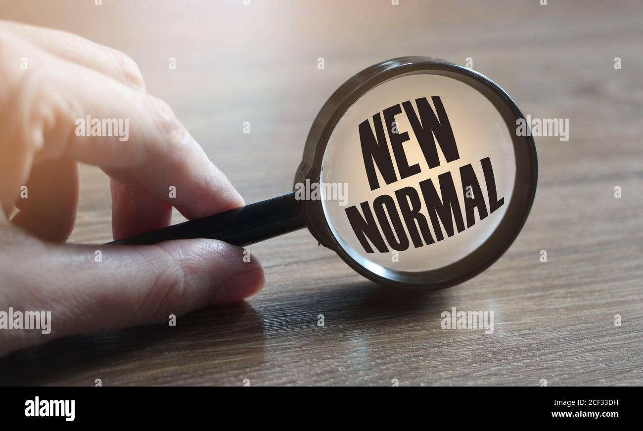 hand holding a magnifying glass with New Normal words under it. Social ...