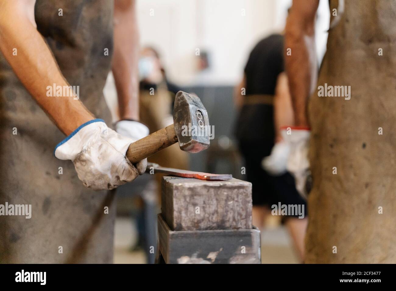 Crop blacksmiths hitting hot metal detail with hammer while forging ...
