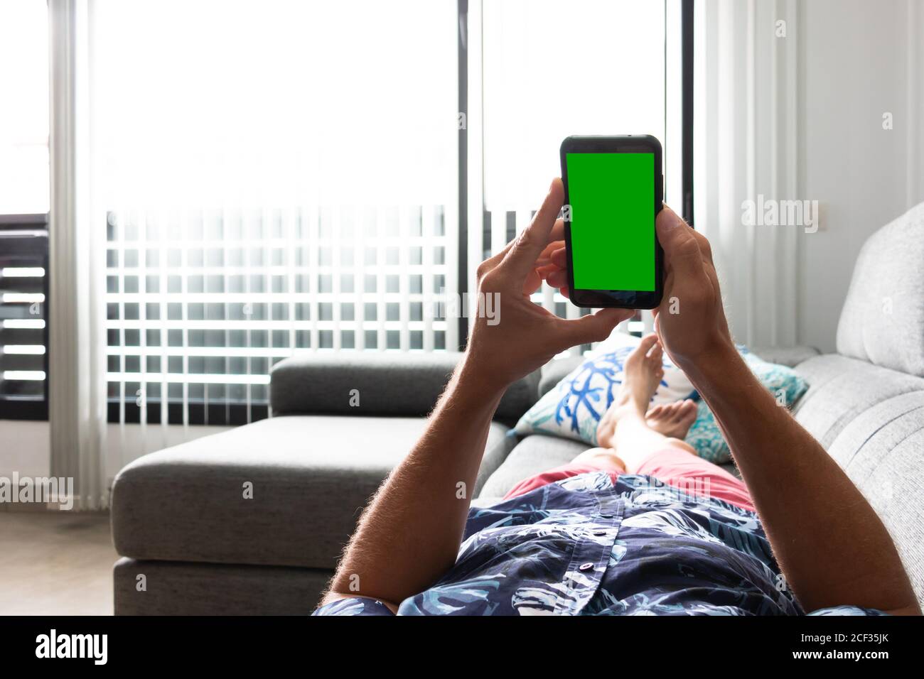 A man lying on a sofa using a smartphone with green screen. Chroma key Stock Photo - Alamy