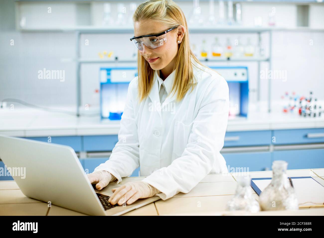 Cute female researcher in white lab coat and protective goggles using ...