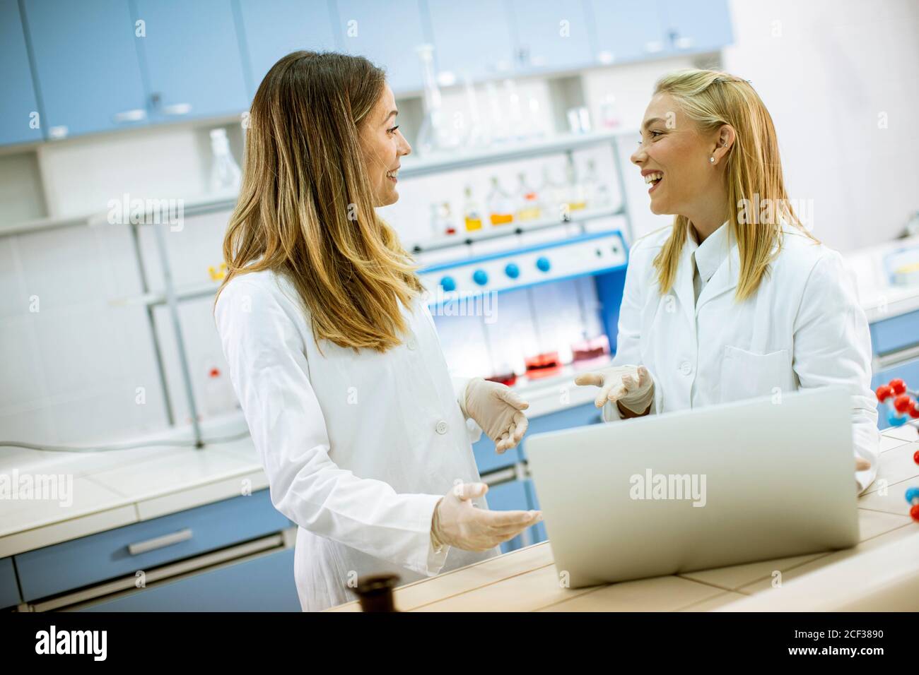 Cute female researchers in white lab coat using laptop while working in ...