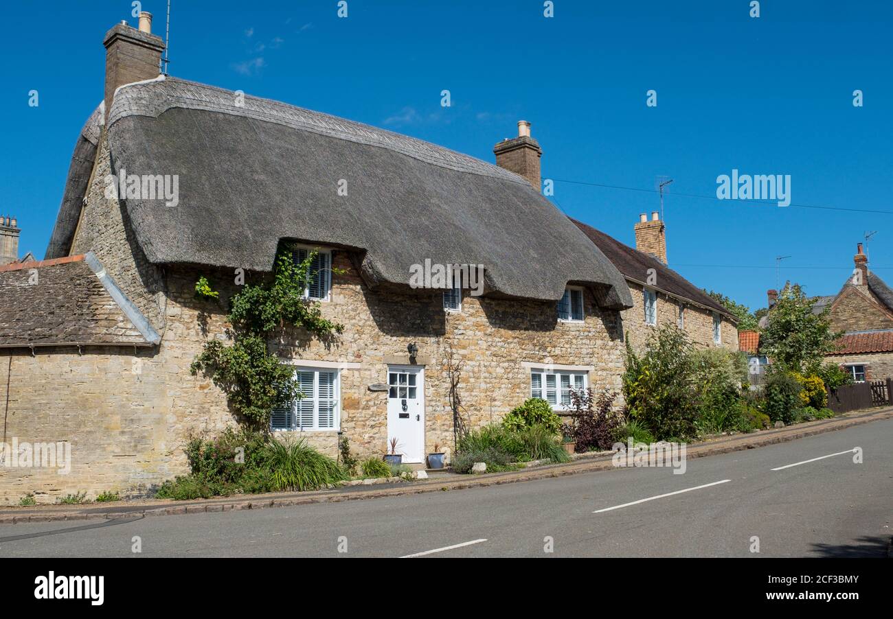 A Typical Northamptonshire Stone House With Thatched Roof Stock Photo a-typical-northamptonshire-stone-house-with-thatched-roof-stock-photo