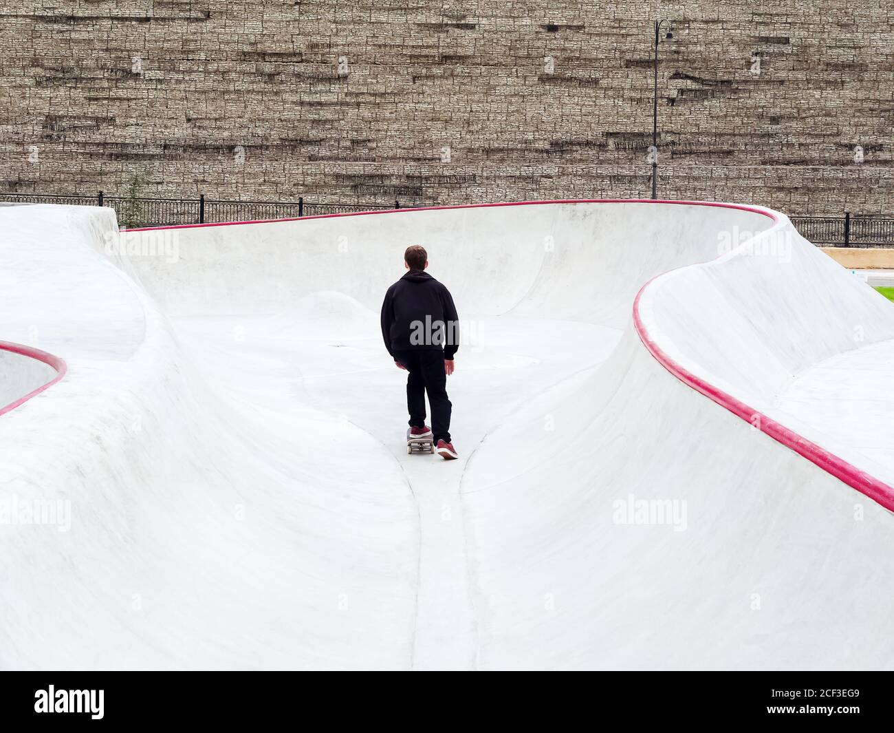 A guy rides a skateboard pushing off with one foot in a concrete ...
