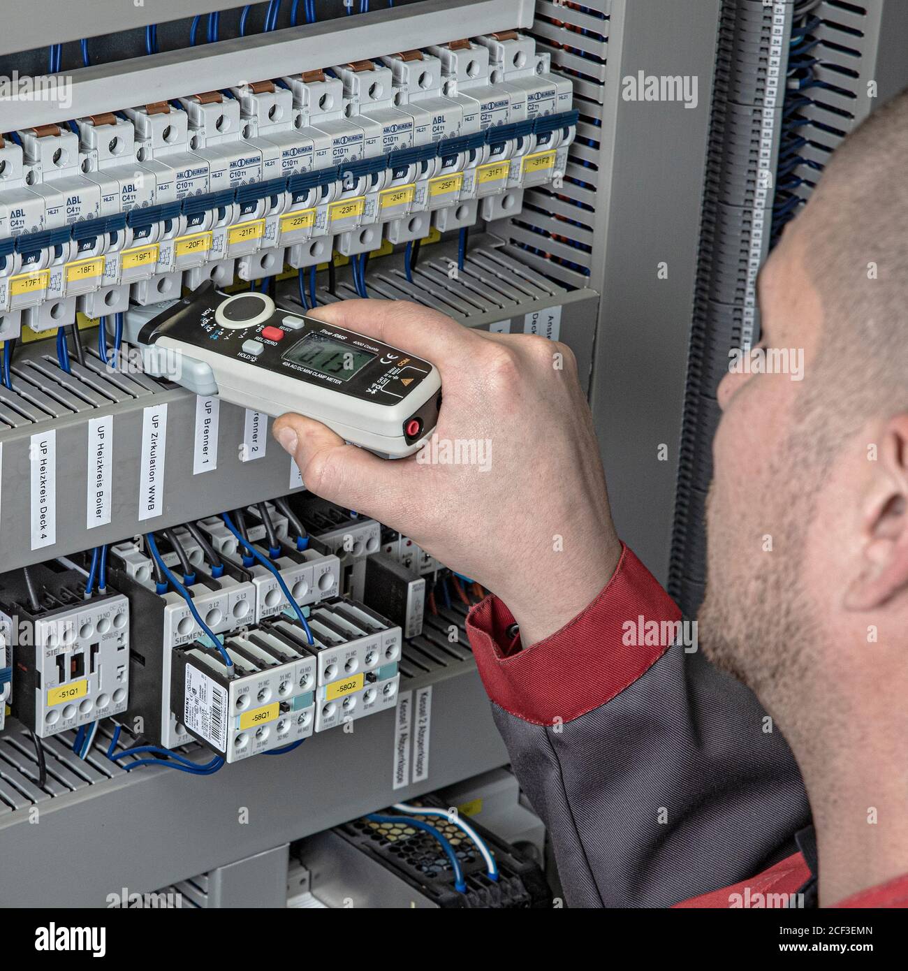 electrician measuring with clamp-multimeter inside a switch cabinet ...