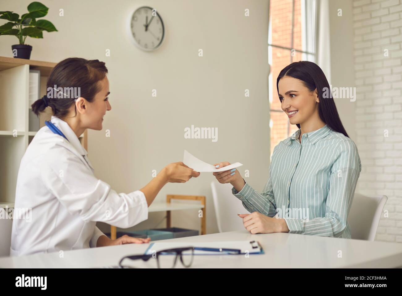 Young smiling doctor giving paper prescription to woman patient in ...