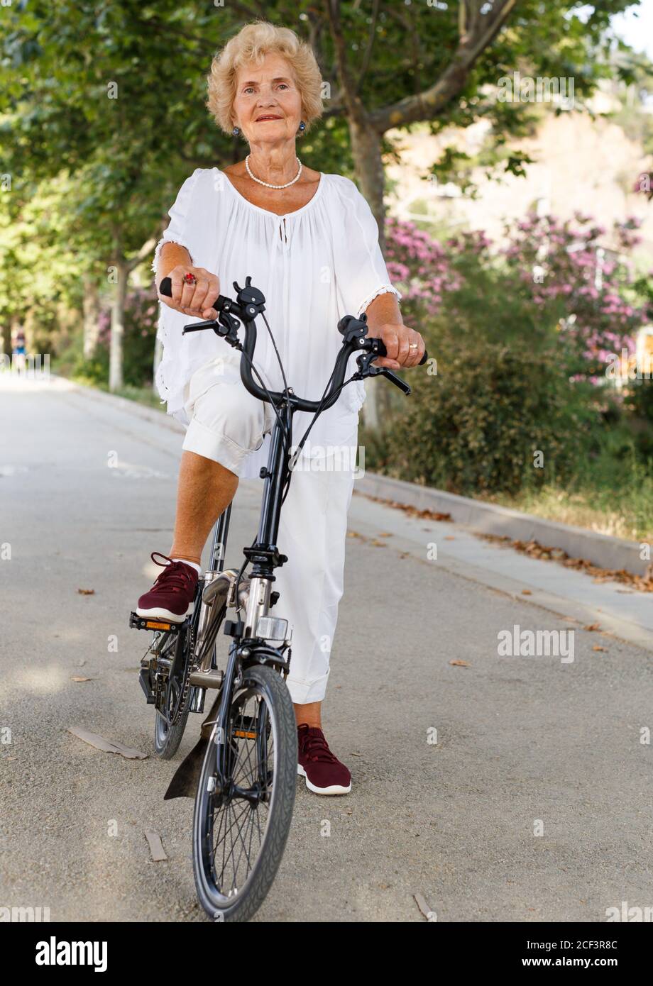 Active elderly woman walking with bike on park path Stock Photo - Alamy