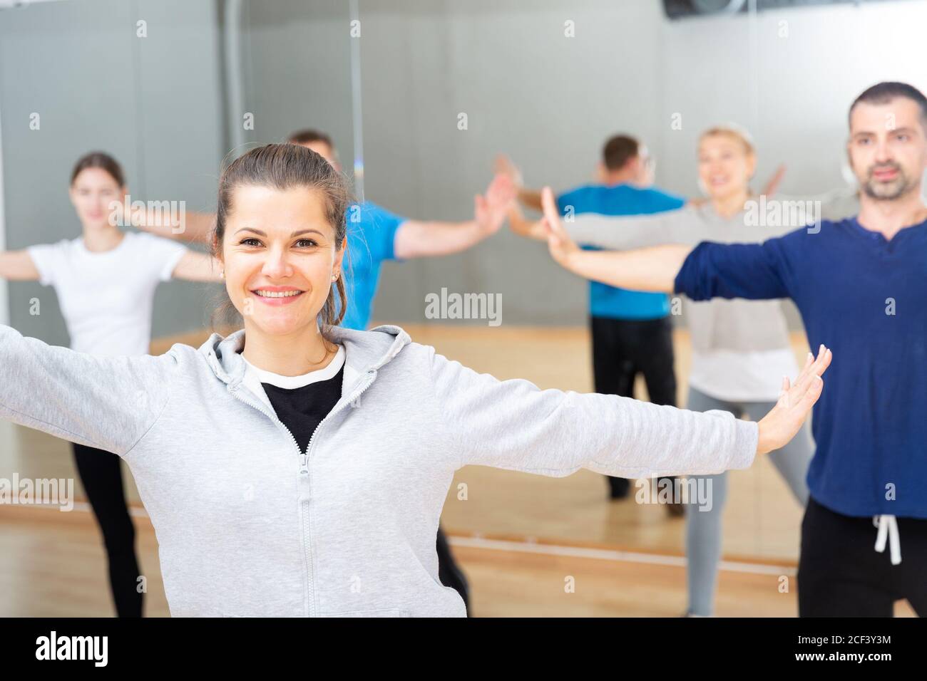 Smiling young female coach doing dance workout with adult group in ...