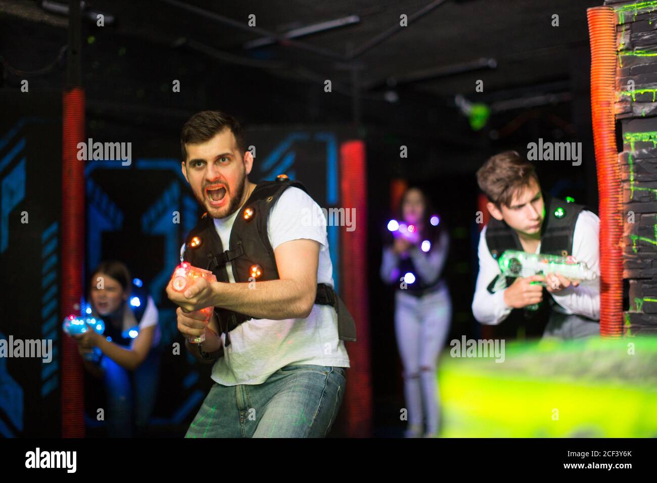 Portrait of young man with laser gun having fun on dark laser tag arena ...