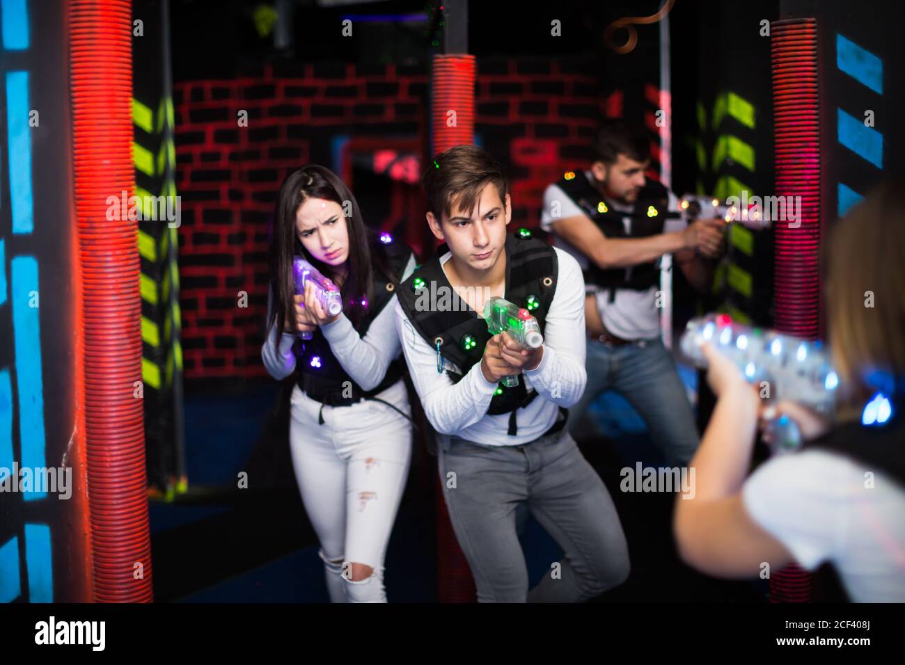 Modern guy and girl aiming laser guns at other players during laser tag ...