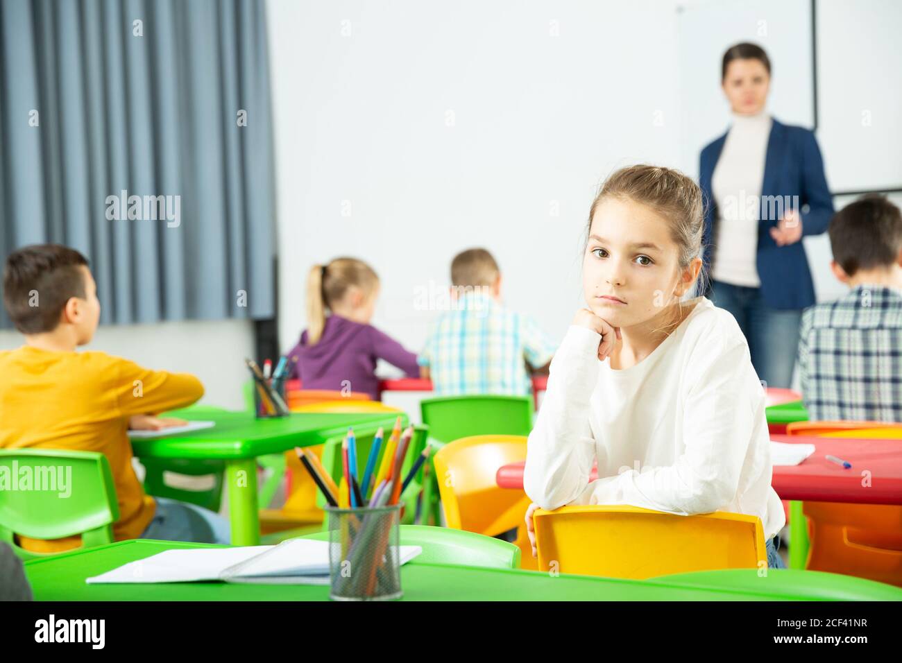 Sad bored schoolgirl sitting separately in classroom during lesson in ...