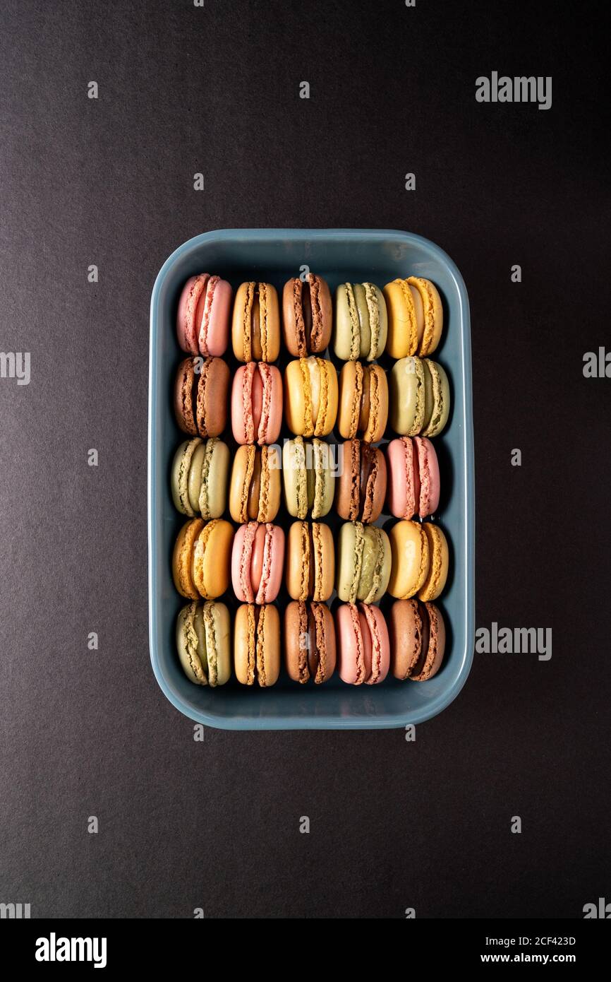 Colorful tasty macaroons displayed inside blue container on black ...