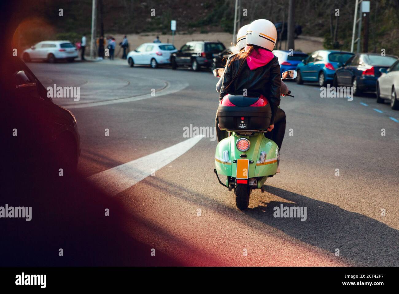 Back view on green scooter with person in helmet driving on asphalt ...