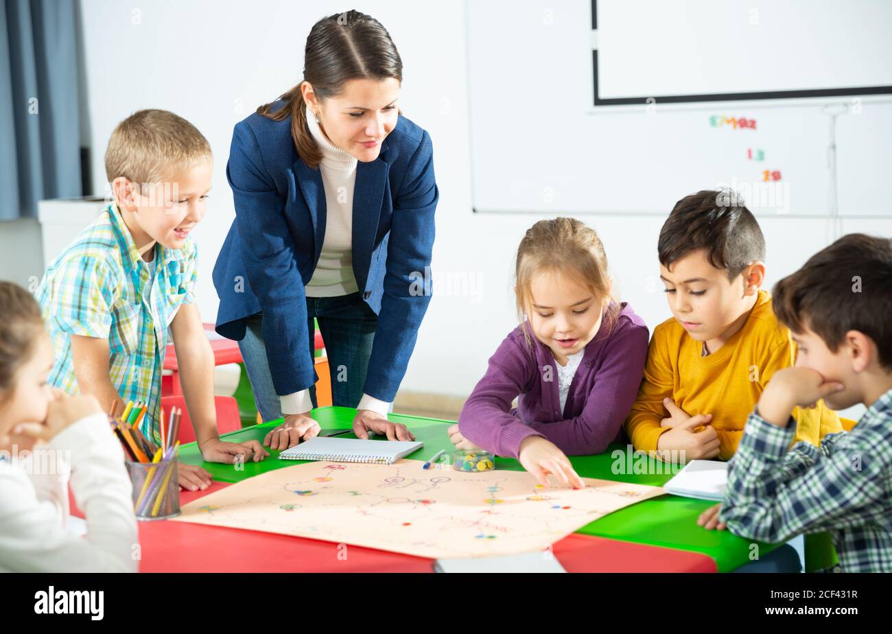 Young female teacher and happy schoolkids playing interesting board ...