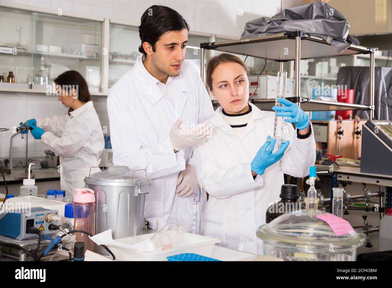 Two young lab technicians discussing while working with reagents in ...