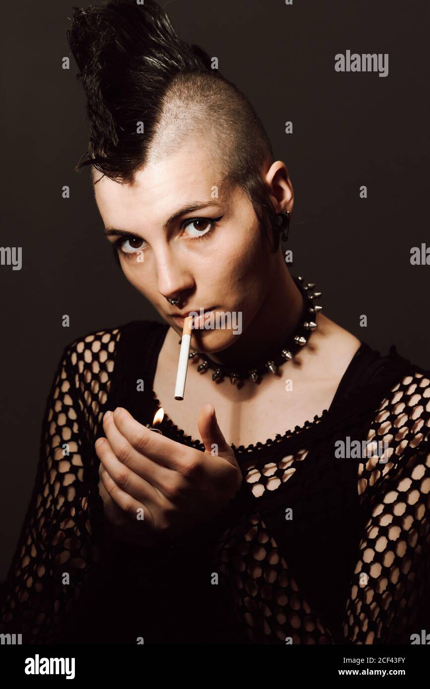 Adult female with mohawk and piercing looking at camera and igniting ...