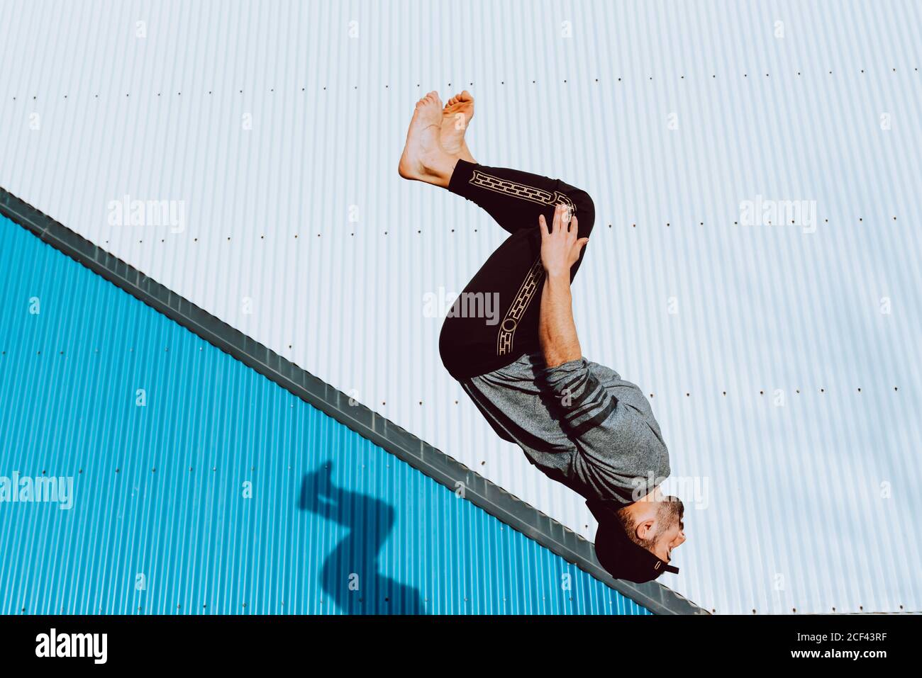 Side view of barefoot guy in stylish outfit performing flip near wall ...