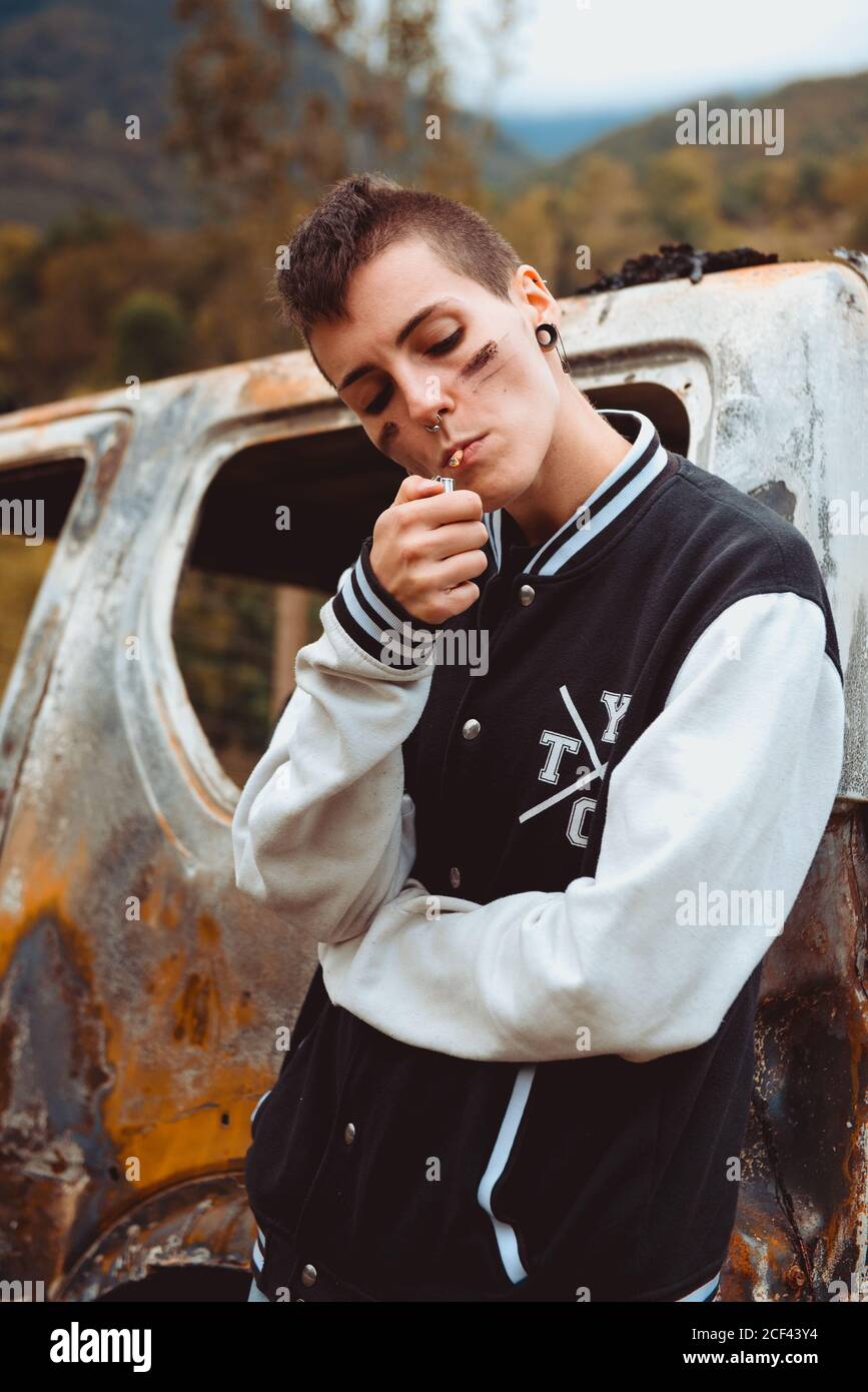 Young female with short hair and painted face lighting cigarette with ...