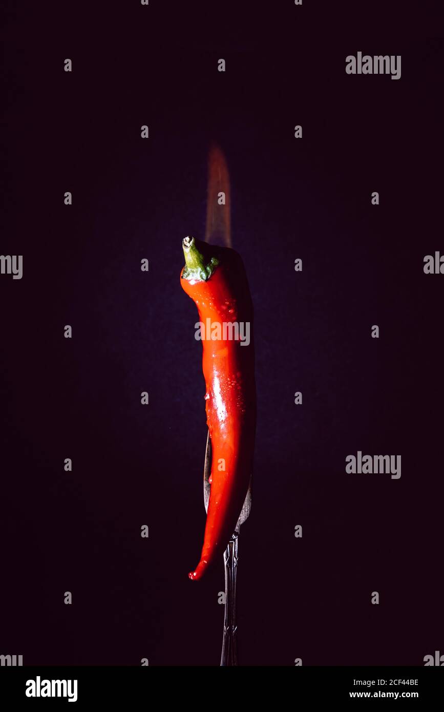 red chili pepper on fire in fork on a black background Stock Photo - Alamy