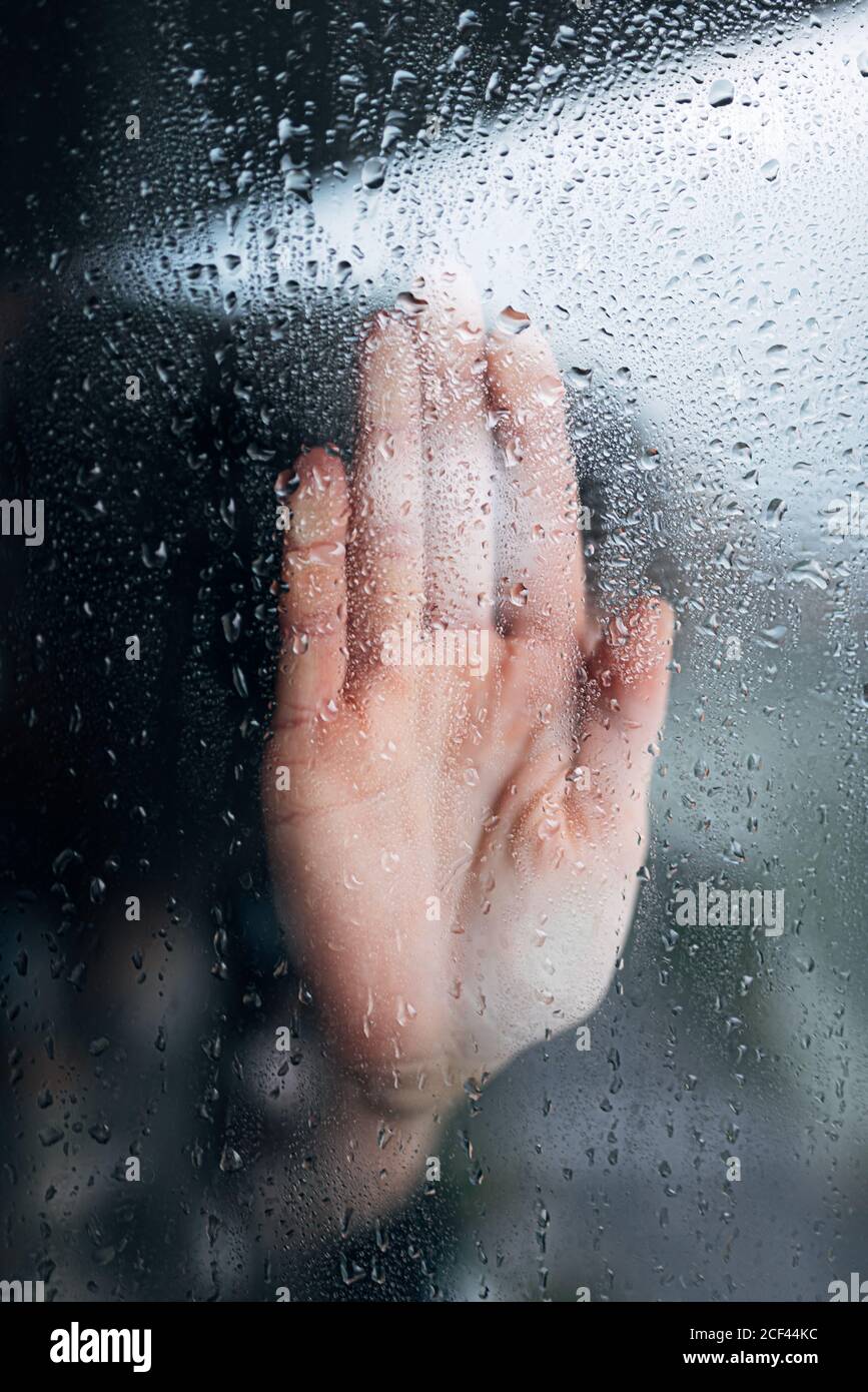 unrecognizable desperate person standing at window and touching wet ...