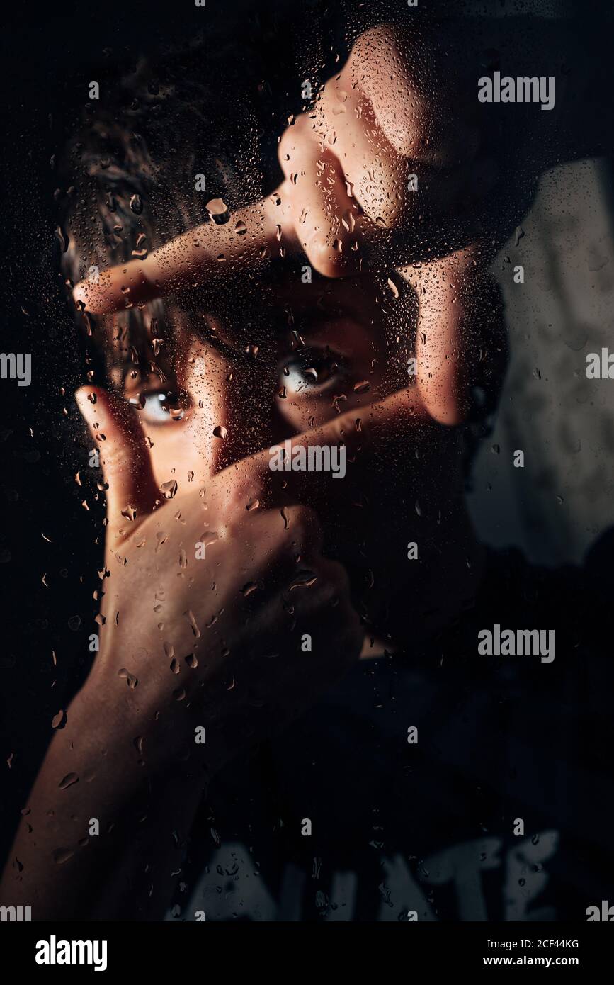 Sad young female making hand frame and looking at camera through wet ...