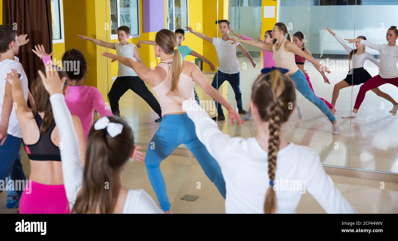 Rear view of group of tweens exercising with female coach in front of ...