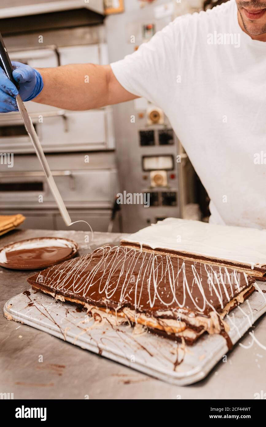 Crop man in latex glove and uniform decorating delicious cake with ...