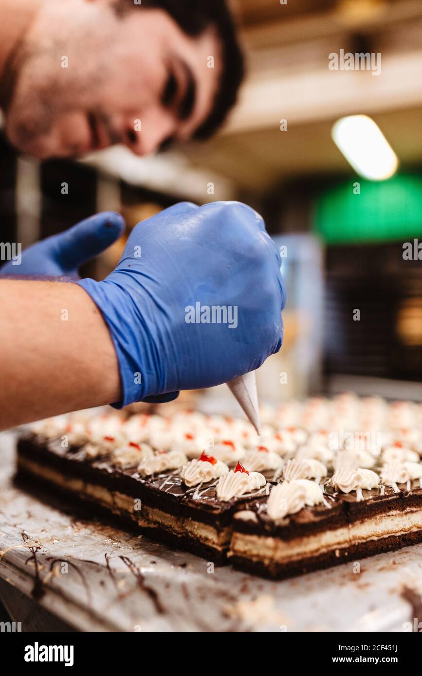 anonymous cook squeezing fresh pastry dough on tray with paper while ...