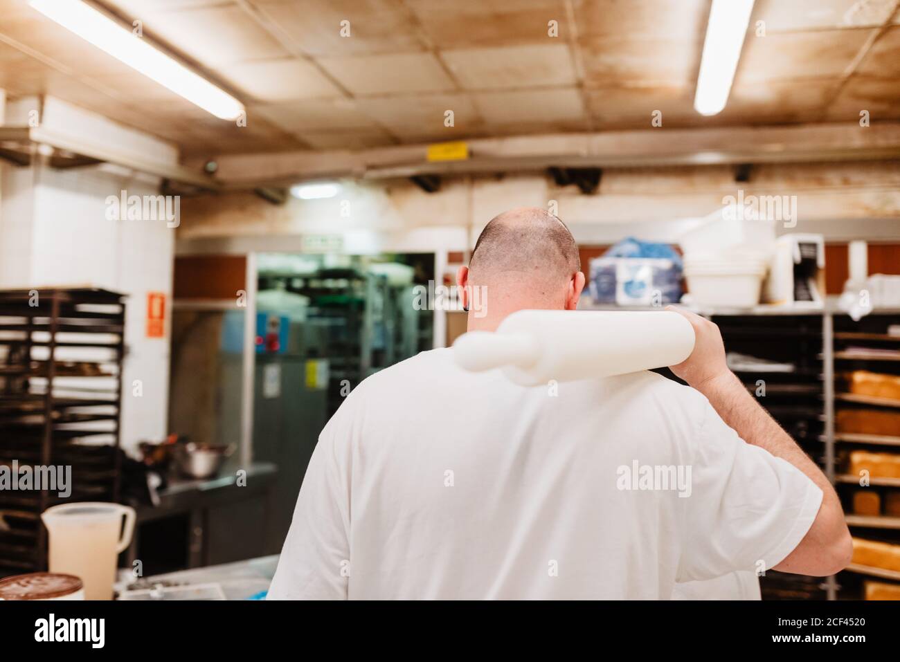 Back view of bald overweight man in white uniform holding rolling pin ...