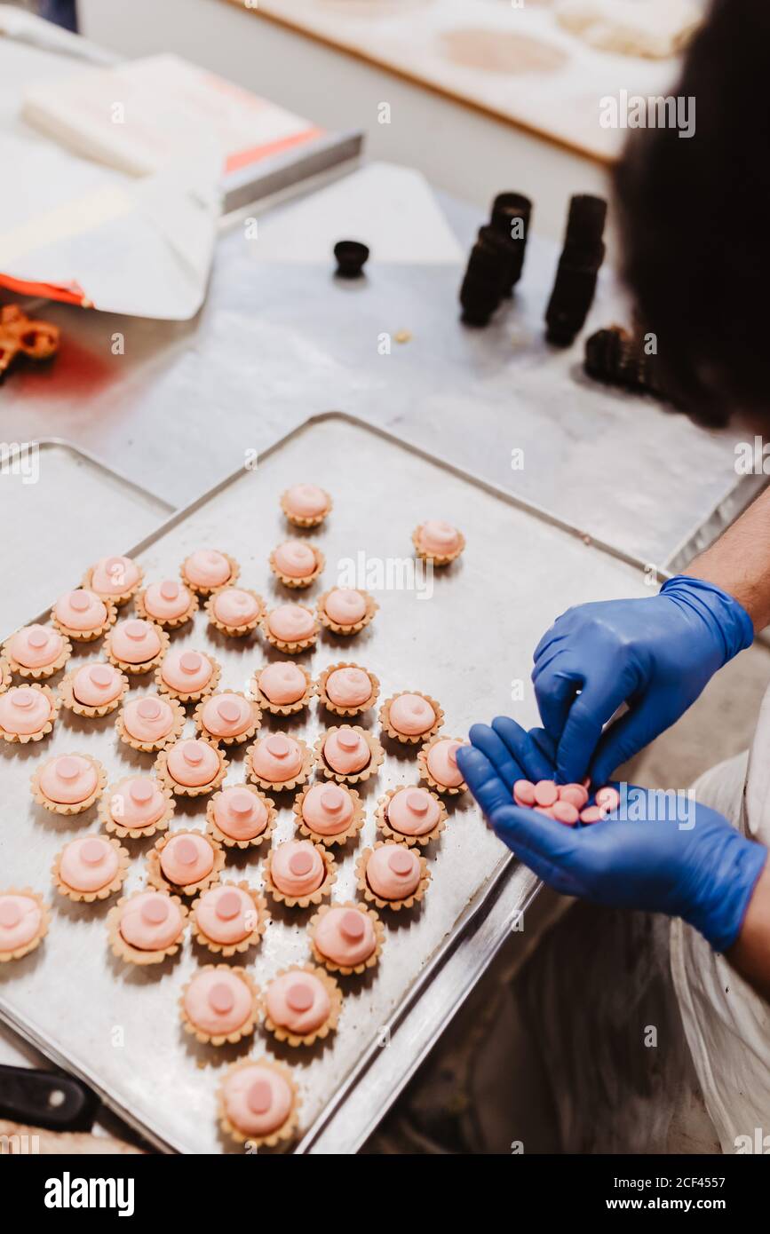 From above unrecognizable confectioner decorating pink pastry on tray ...