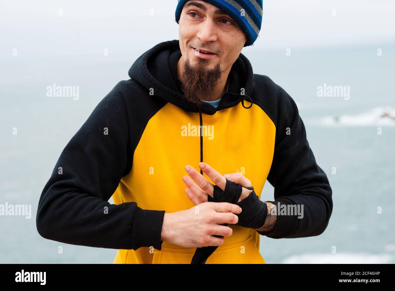 Bearded adult man wrapping bandage around hand while standing against ...