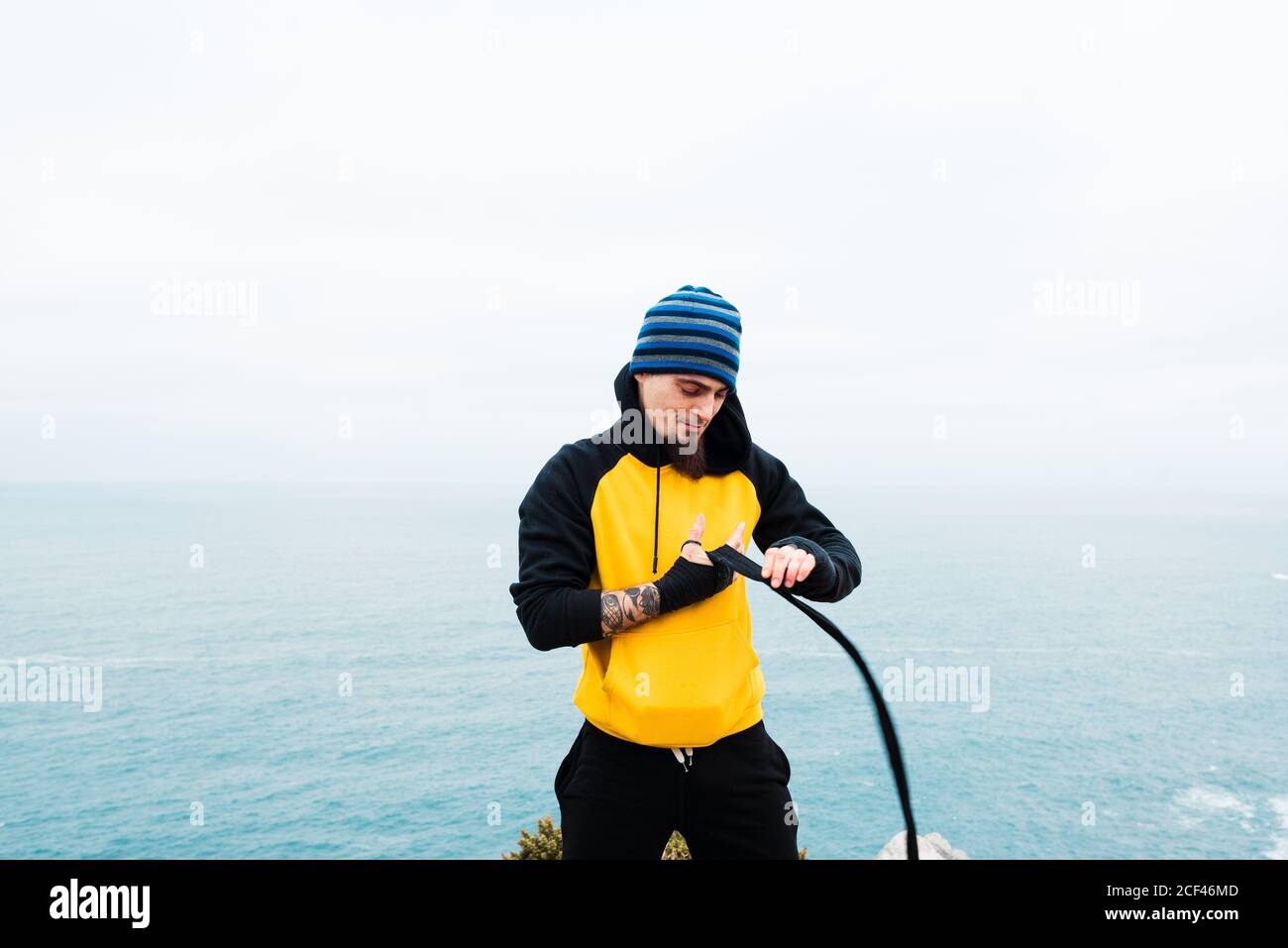 Bearded adult man wrapping bandage around hand while standing against ...