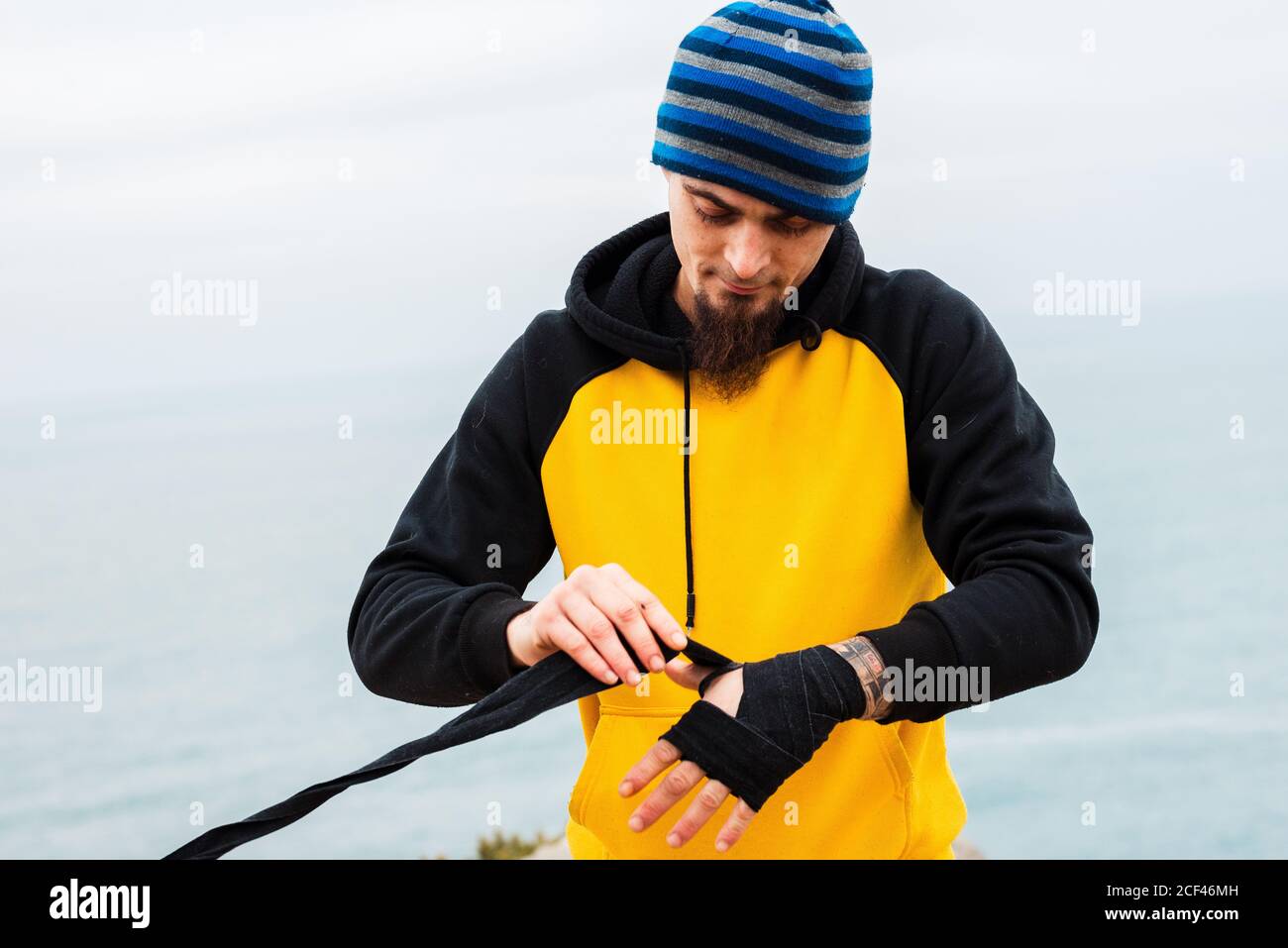 Bearded adult man wrapping bandage around hand while standing against ...